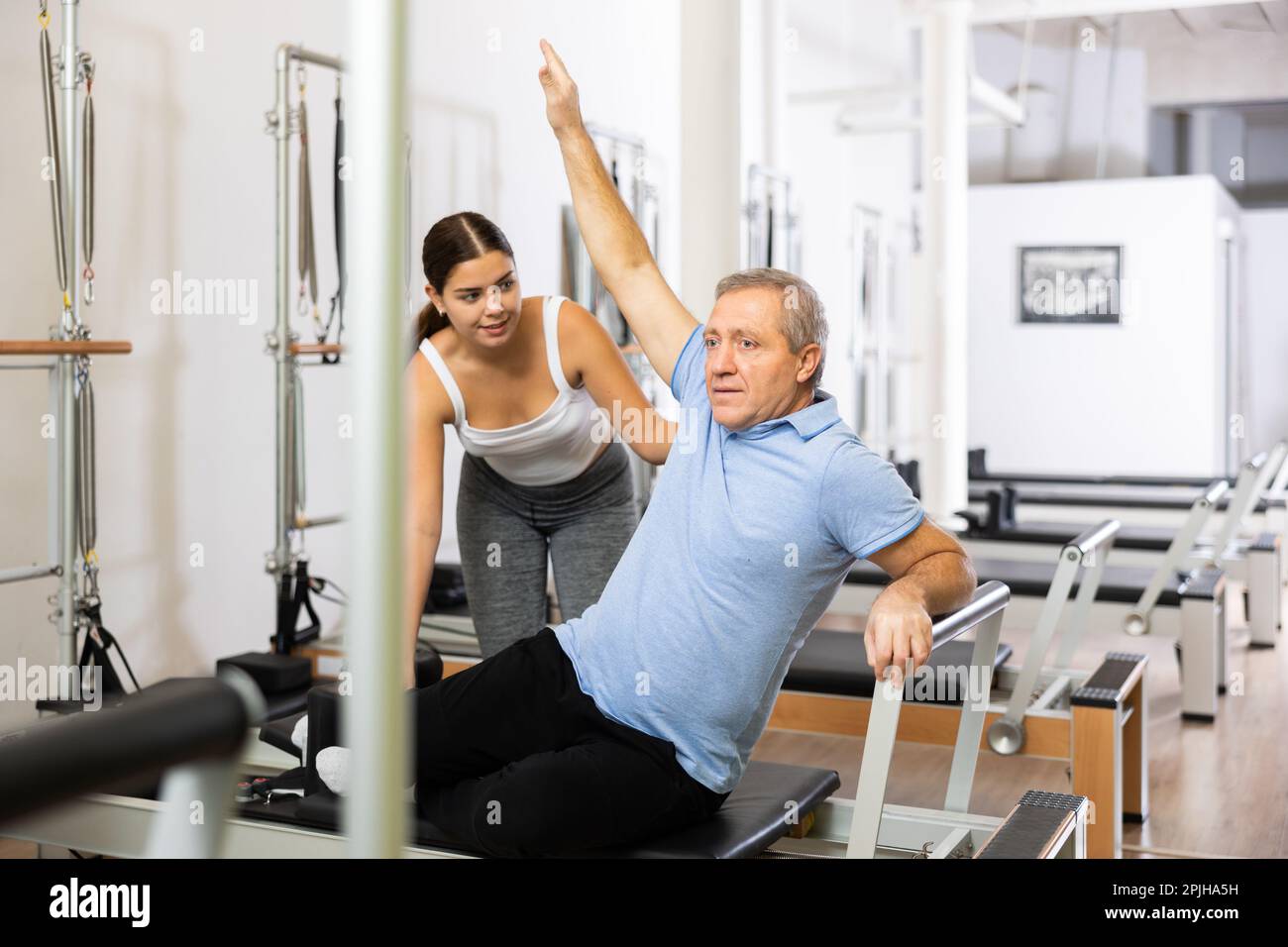 Focused old man practicing stretching Pilates exercise with personal ...