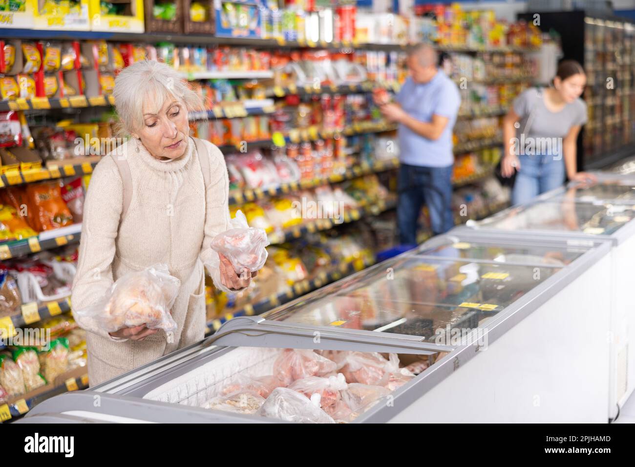 Mature woman choosing frozen food in supermarket. Young woman ...