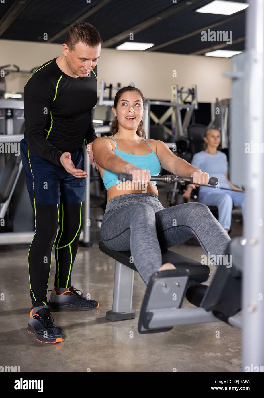 Male fitness instructor showing young woman how to use cable row ...