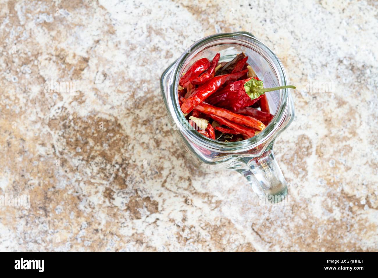 Looking down at a glass jar full of bright red dried cayenne peppers ...