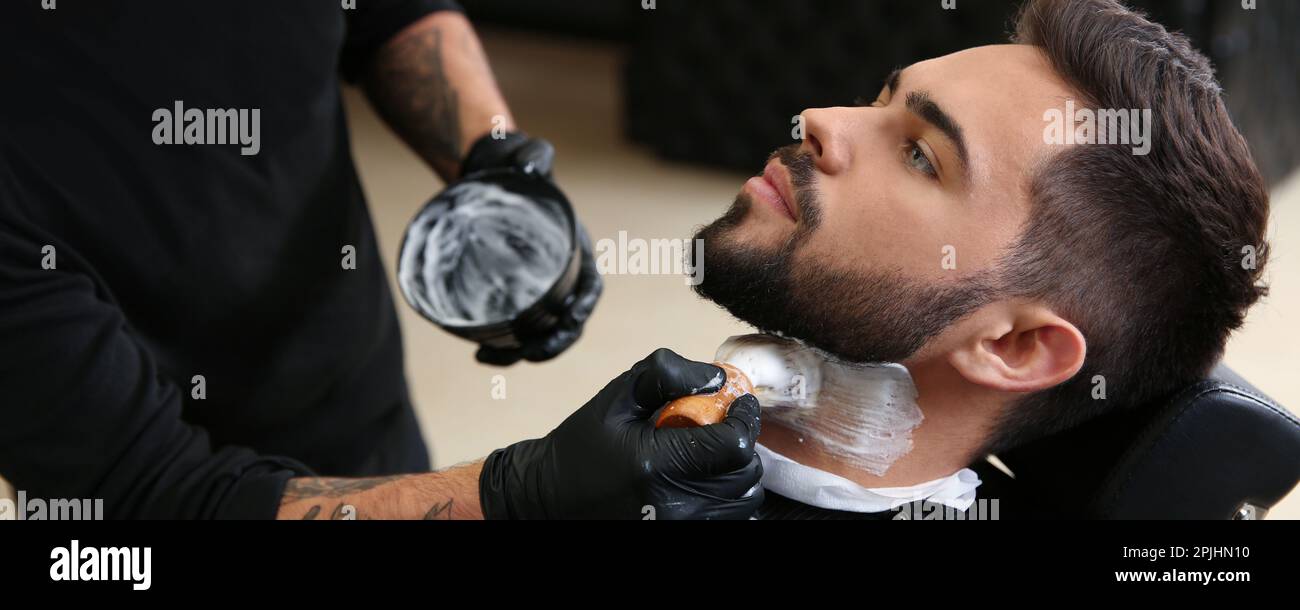 Professional hairdresser applying shaving foam onto client's skin in ...