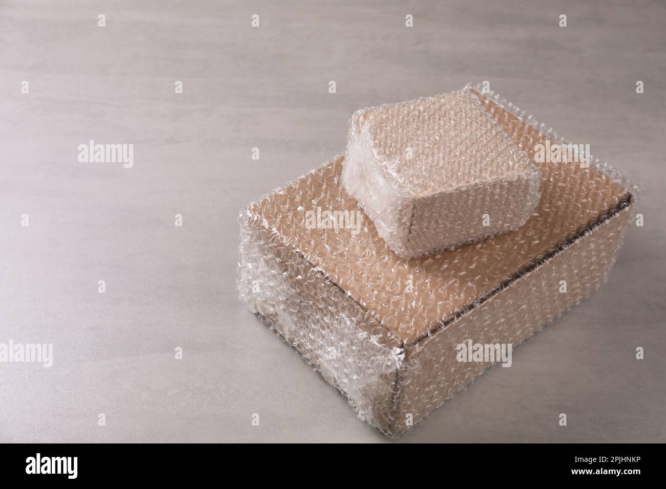 Cardboard boxes covered with bubble wrap on light grey table. Space for ...