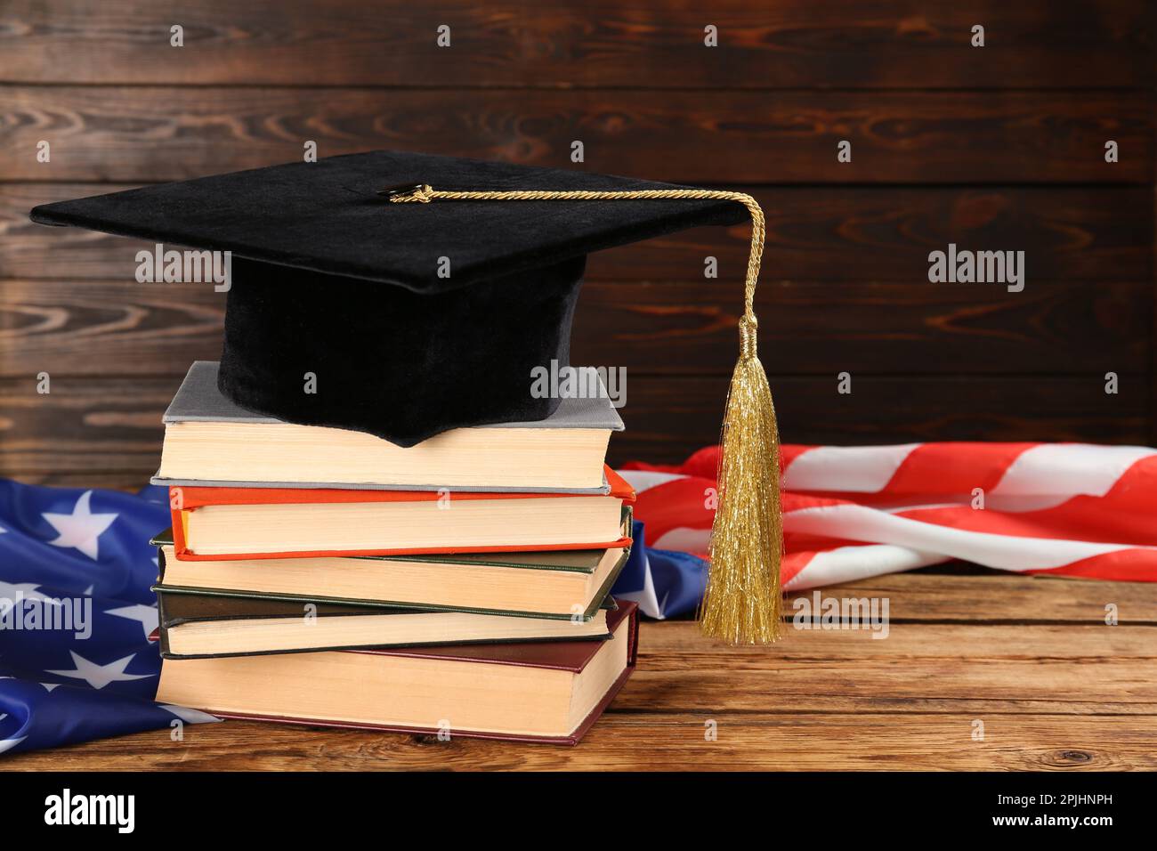 Graduation hat, books and American flag on wooden table. Space for text ...