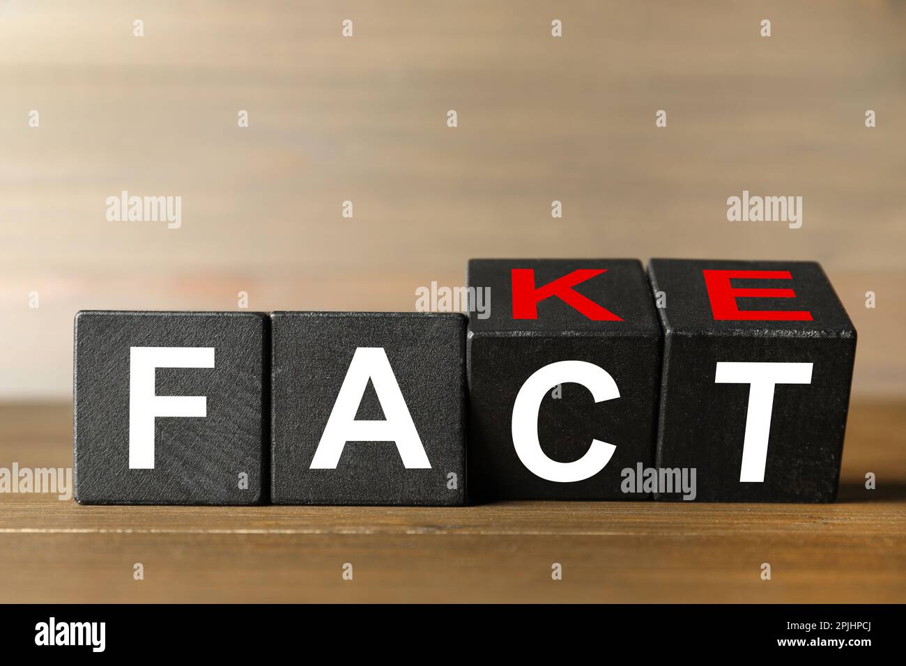 Words FAKE and FACT made with black cubes on wooden table, closeup ...