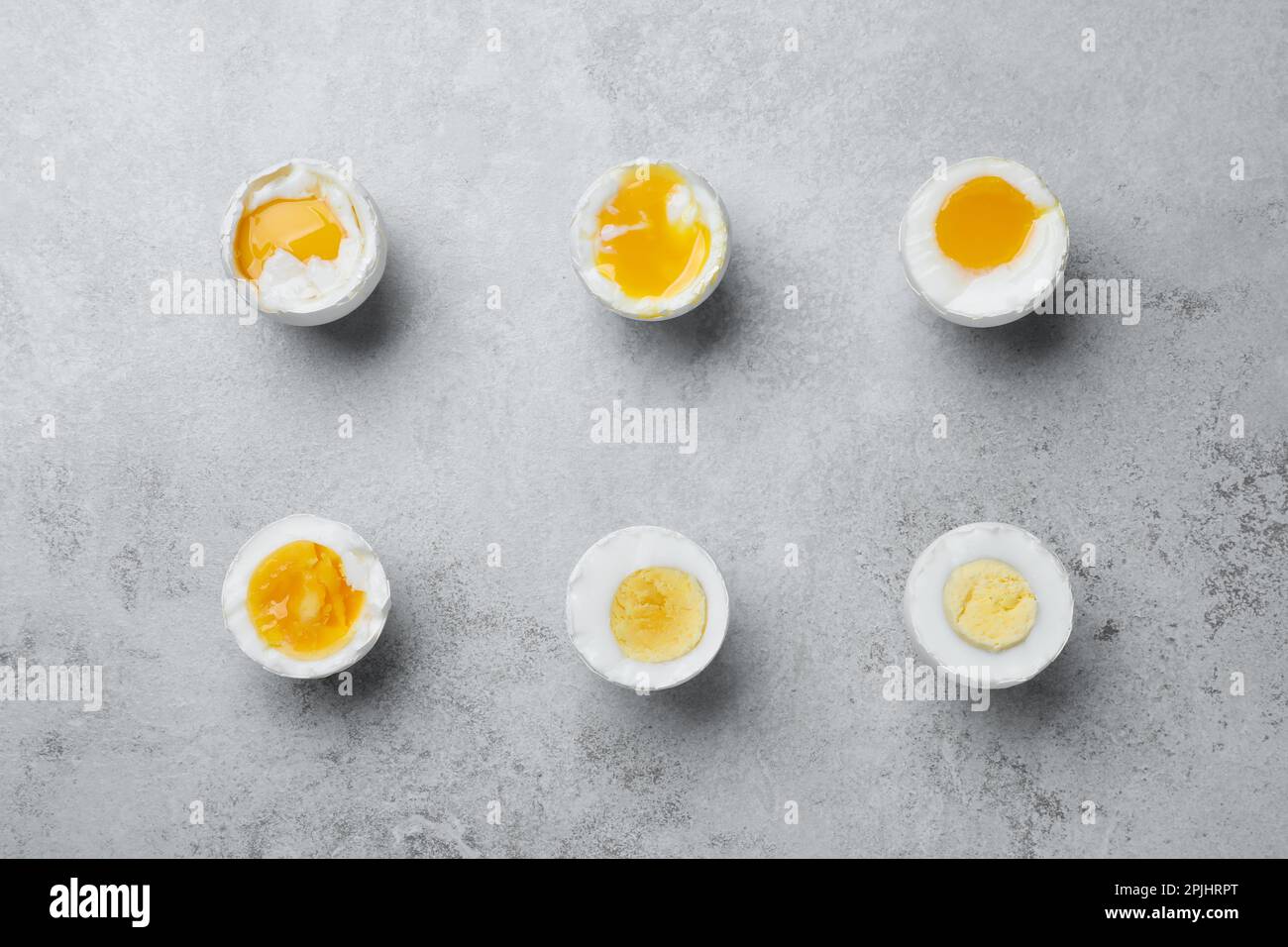 Different readiness stages of boiled chicken eggs on light grey table ...