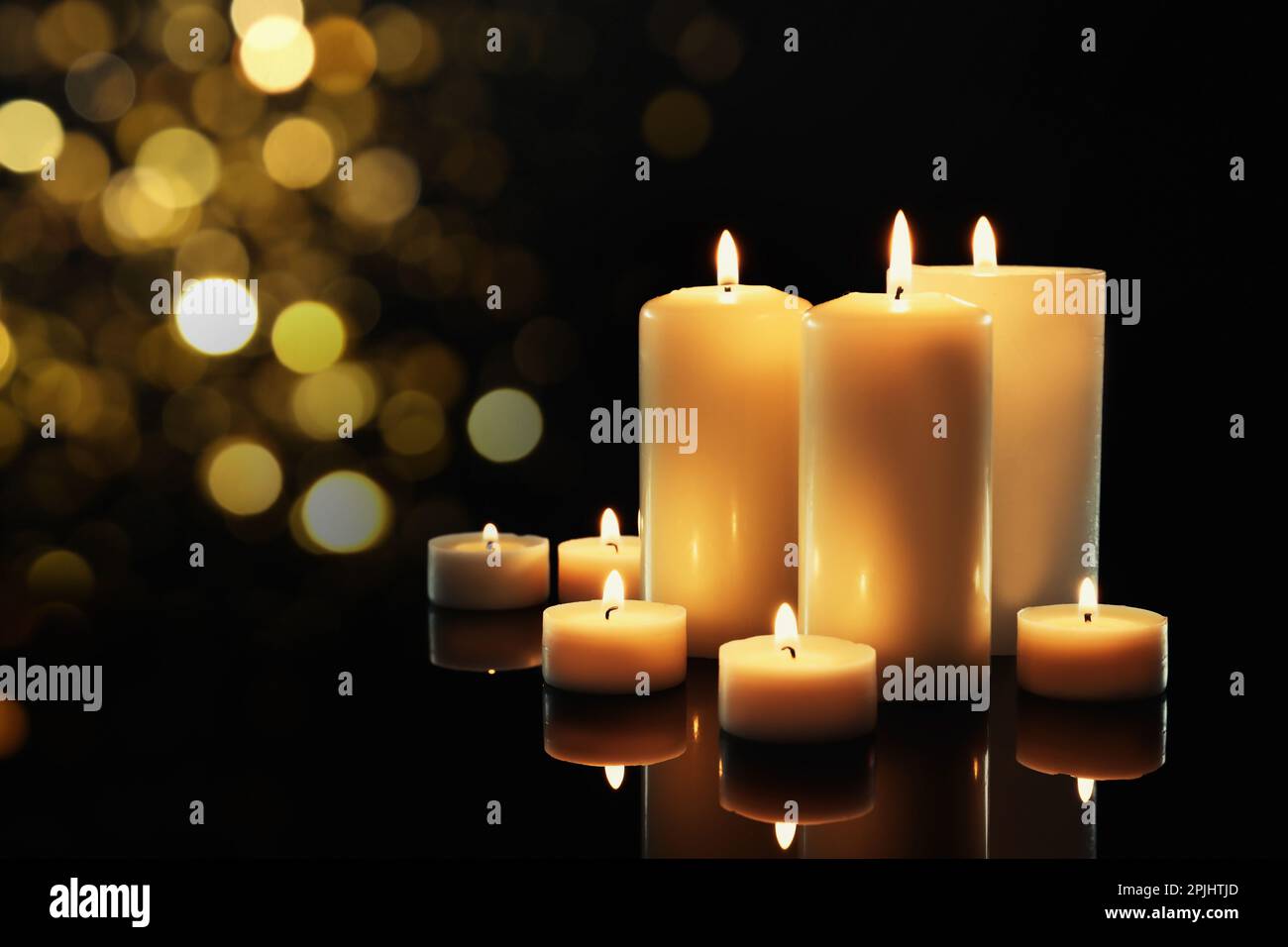 Different wax candles burning on table against dark background with blurred lights. Bokeh effect ...