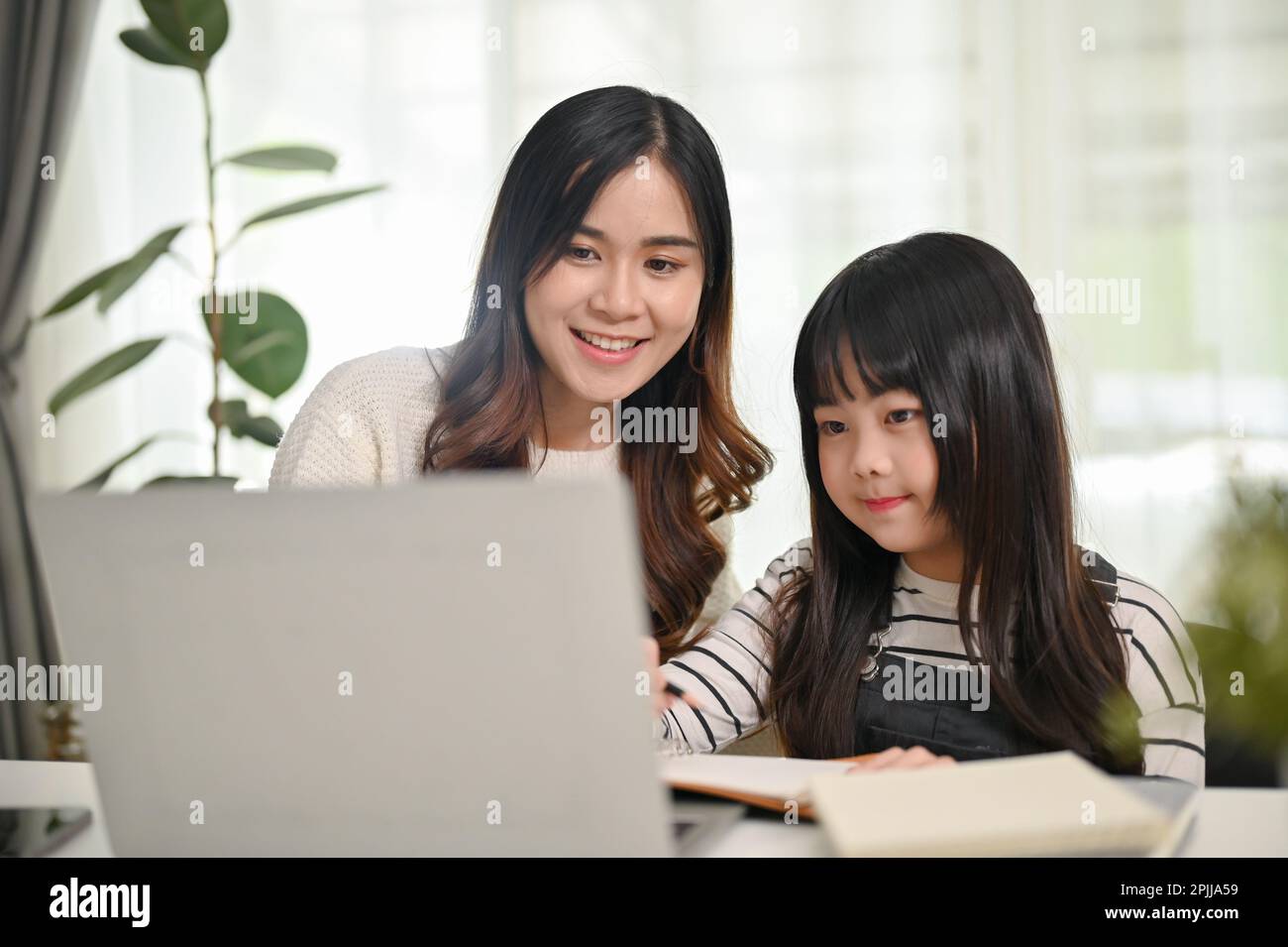 Kind and happy Asian sister helping her little sister with online study ...