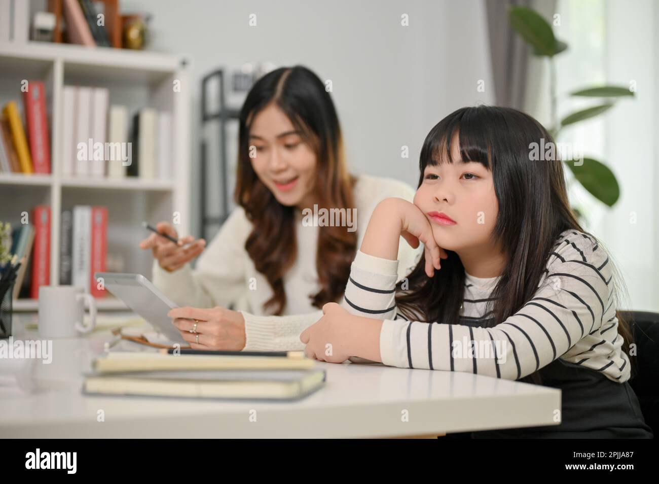 Lazy and bored young Asian girl sits at a table with her hand on her ...