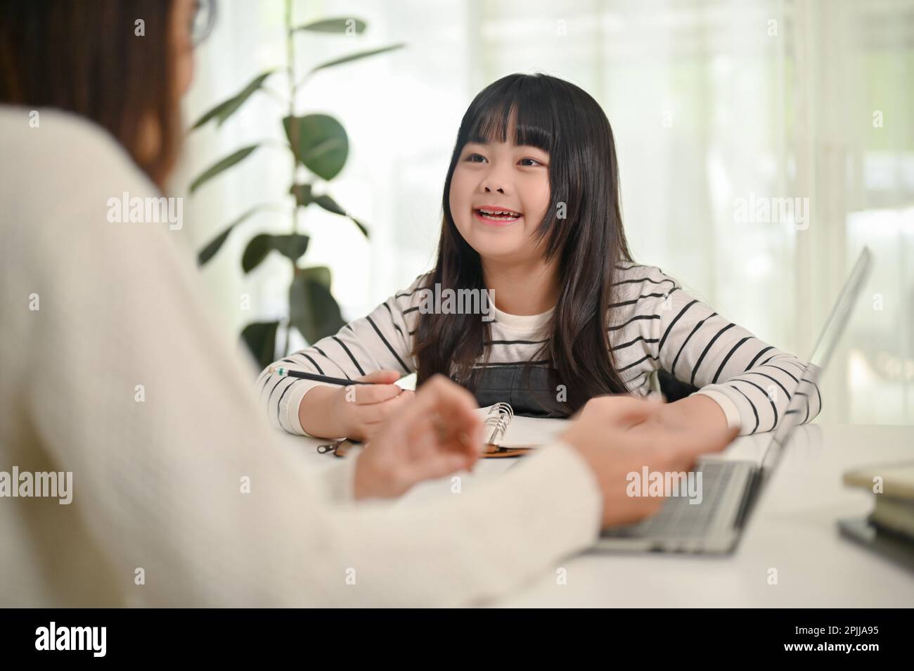 An adorable young Asian girl studying at home asks a question while her ...
