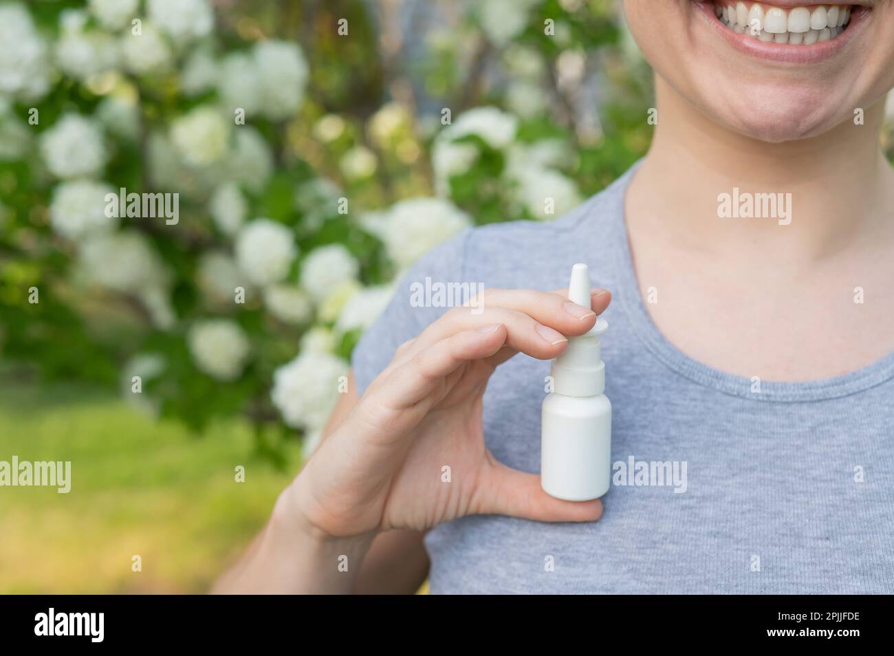 Happy woman demonstrating nasal spray on the background of a blossoming ...