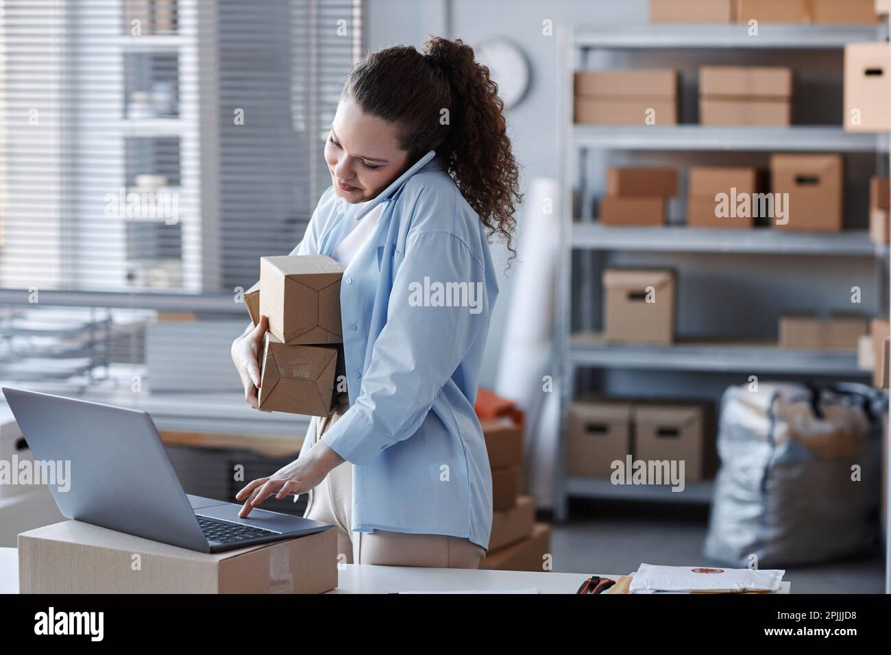 Young busy female worker of post office talking on mobile phone and ...