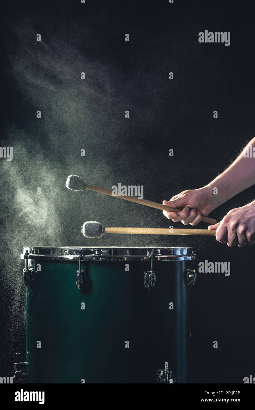 A man plays a musical percussion instrument with sticks on a dark ...