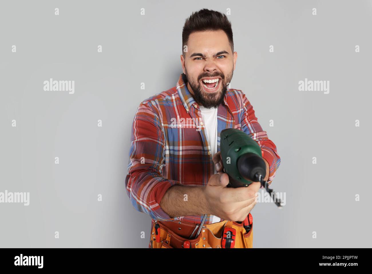Emotional man with power drill on grey background Stock Photo - Alamy