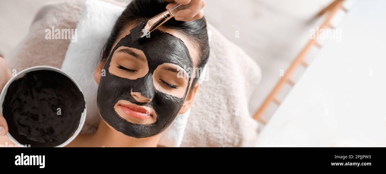 Cosmetologist applying black mask onto woman's face in spa salon, top ...