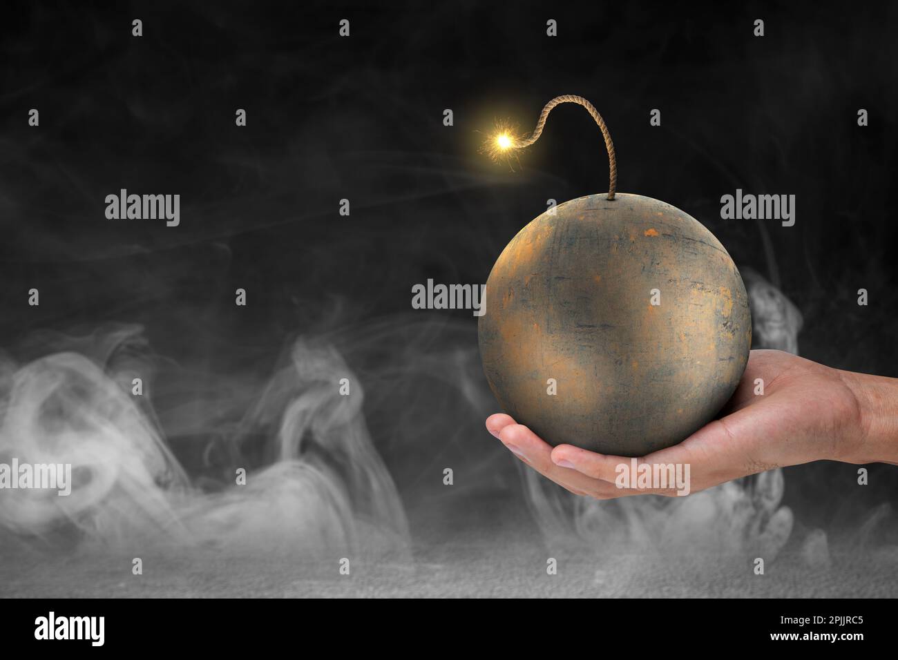 A human hand holding a ball bomb with a burning fuse on dark background ...