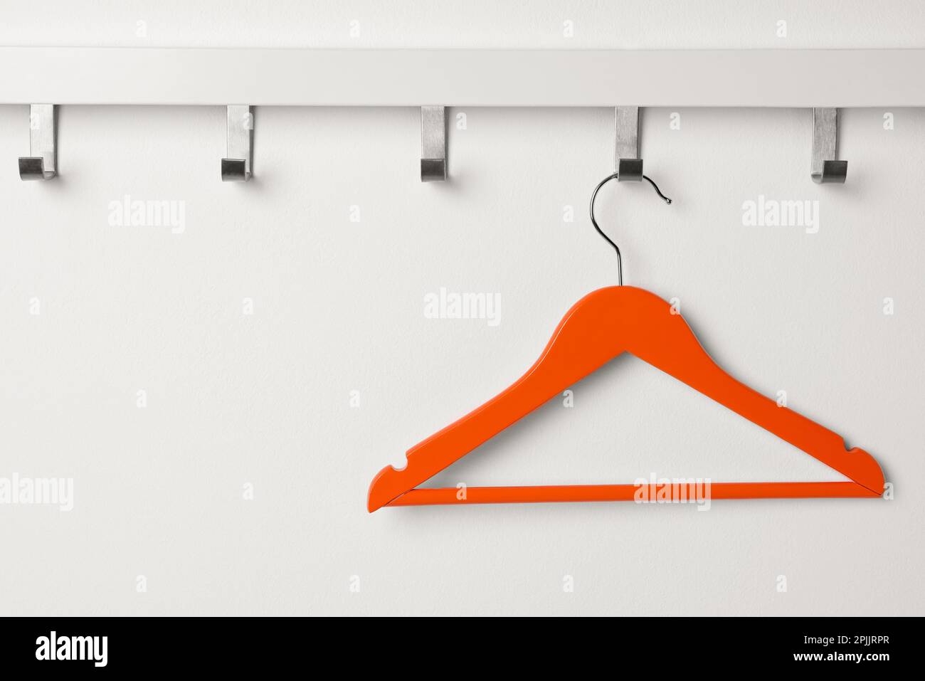Rack with empty orange clothes hanger on white wall Stock Photo - Alamy