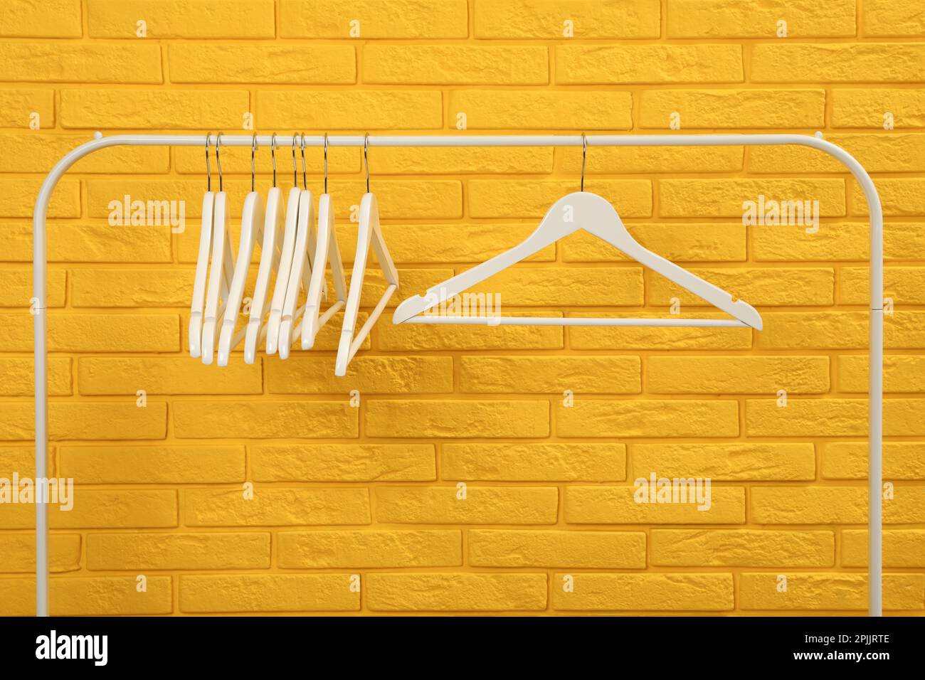Wardrobe rack with many hangers near yellow brick wall Stock Photo - Alamy