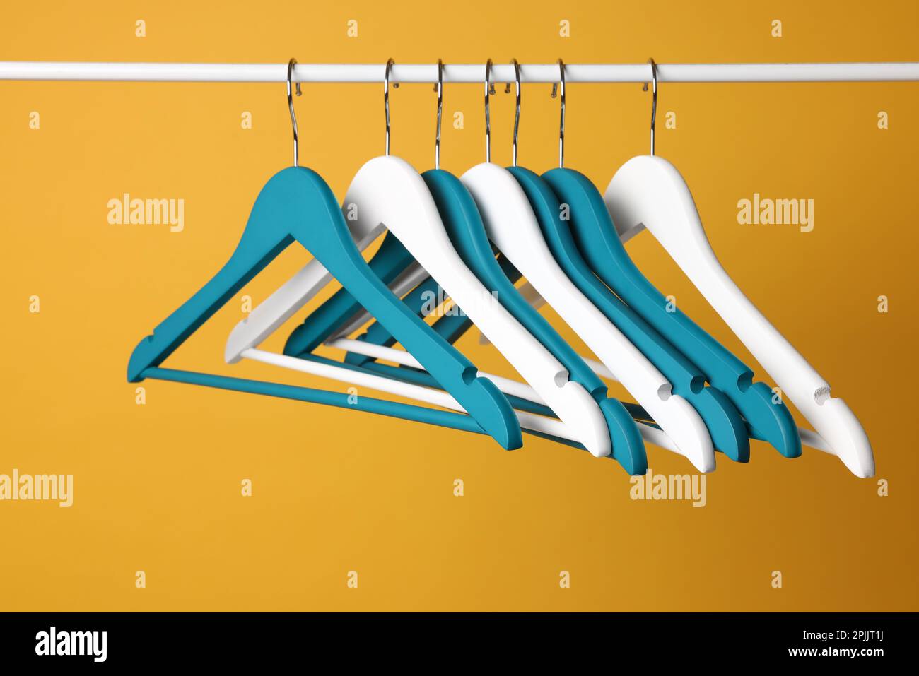 Empty clothes hangers on metal rail against yellow background Stock ...