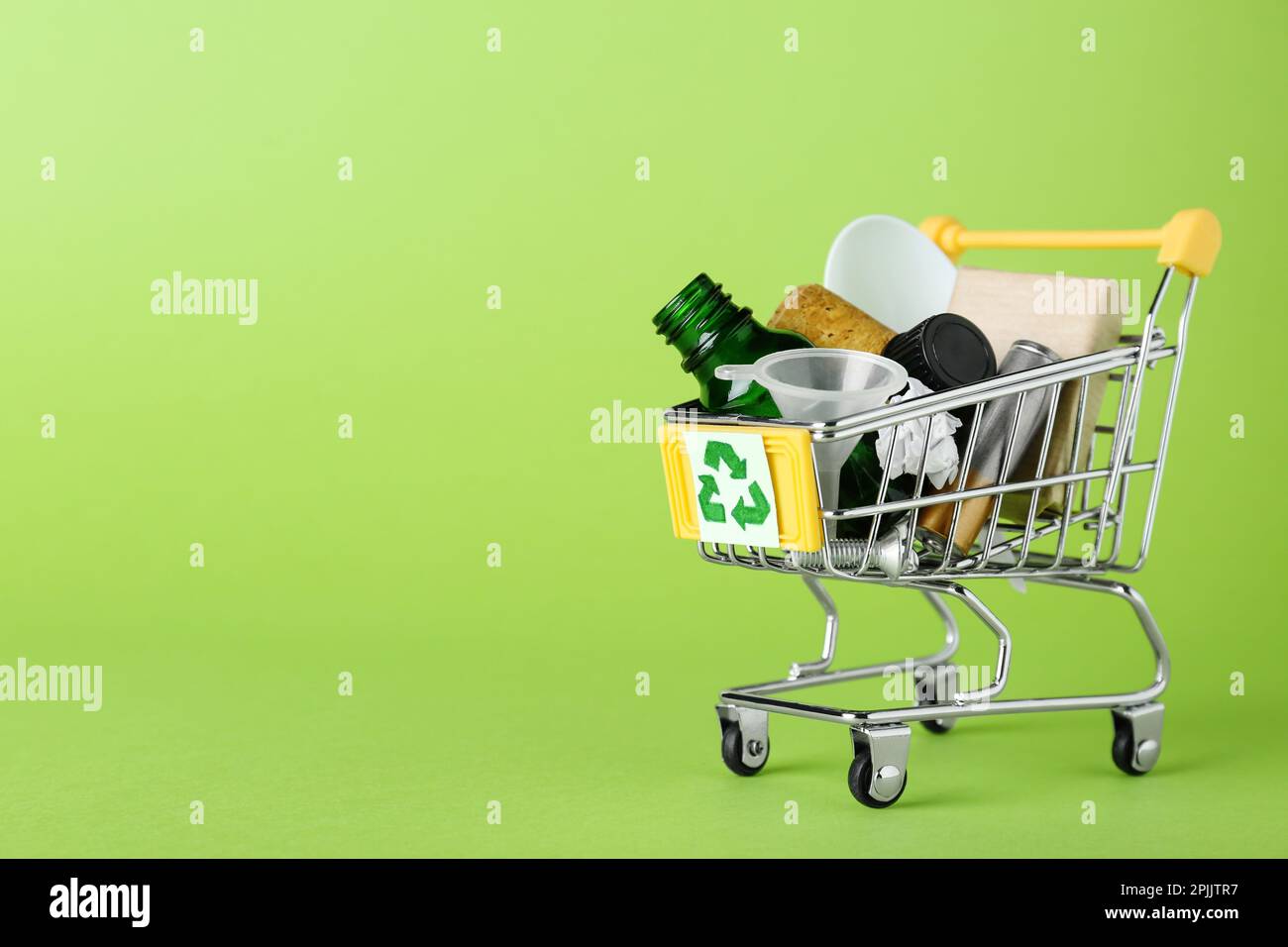 Shopping cart with recycling symbol full of garbage on light green ...