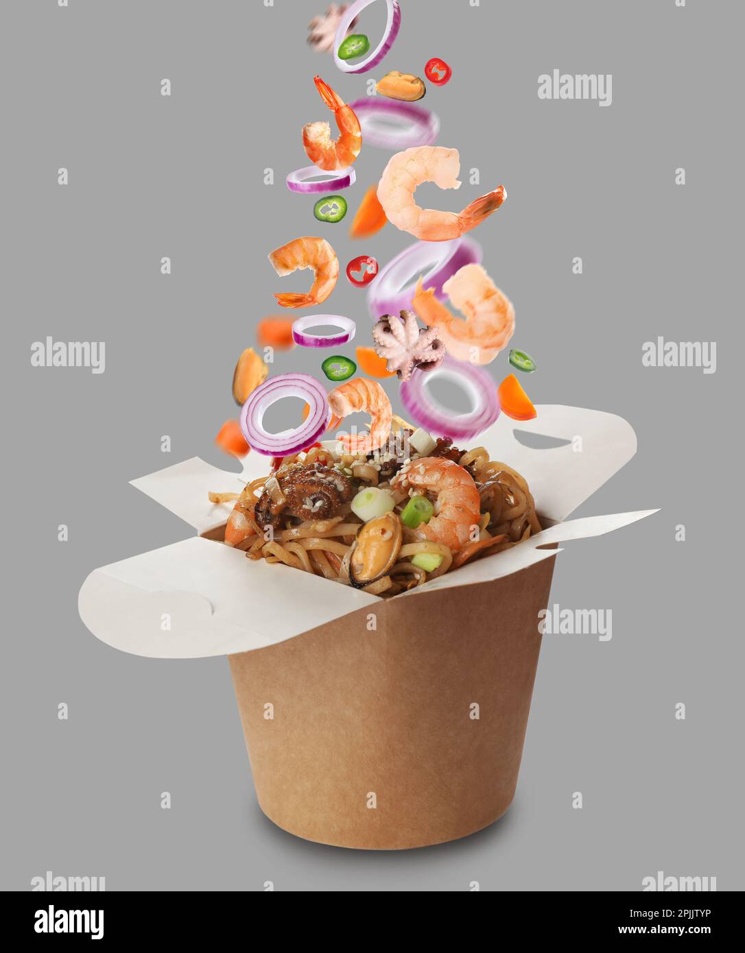 DIfferent fresh ingredients falling into box of wok noodles on grey ...
