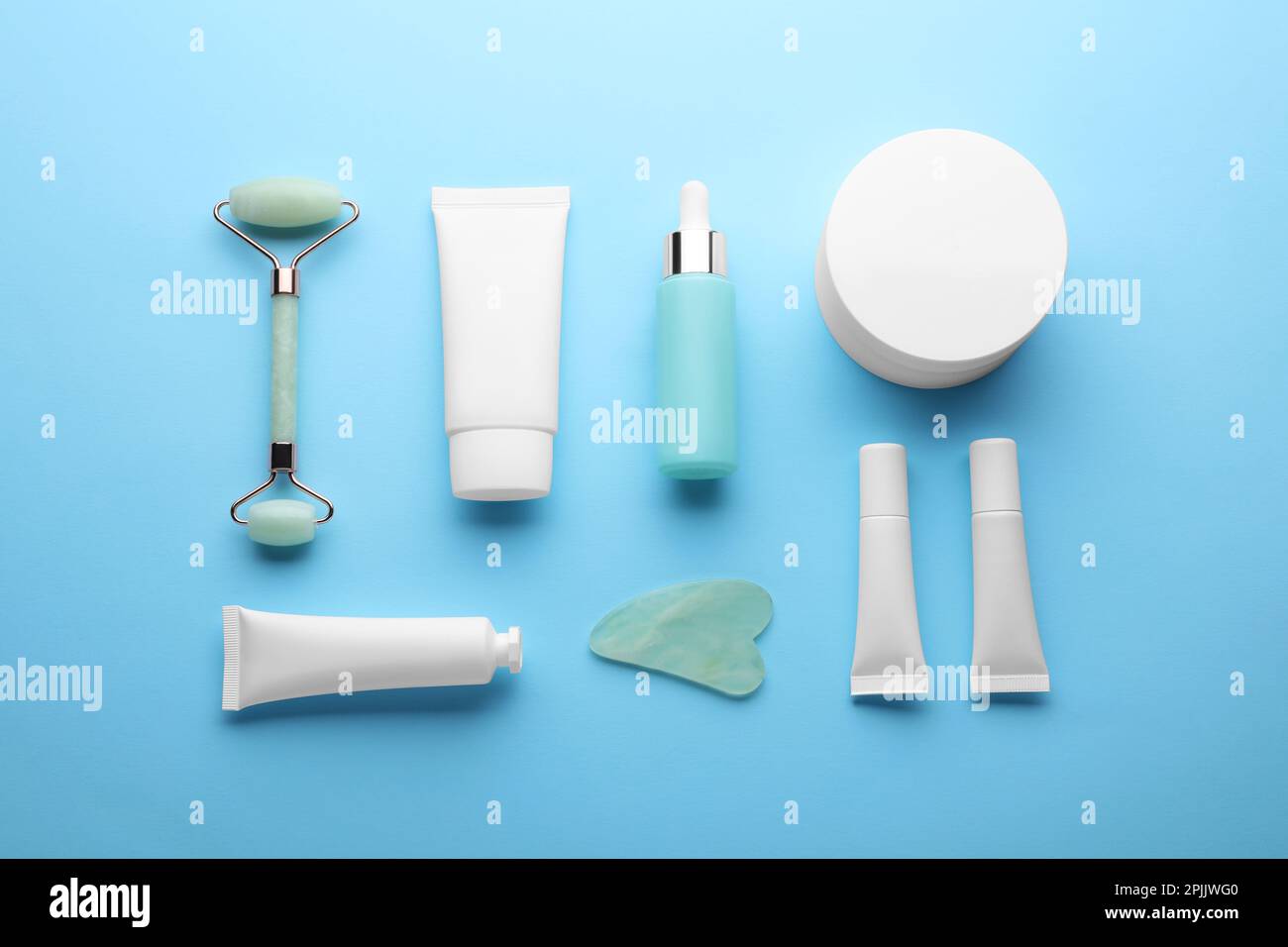 Natural face roller, gua sha tool and cosmetic products on light blue ...