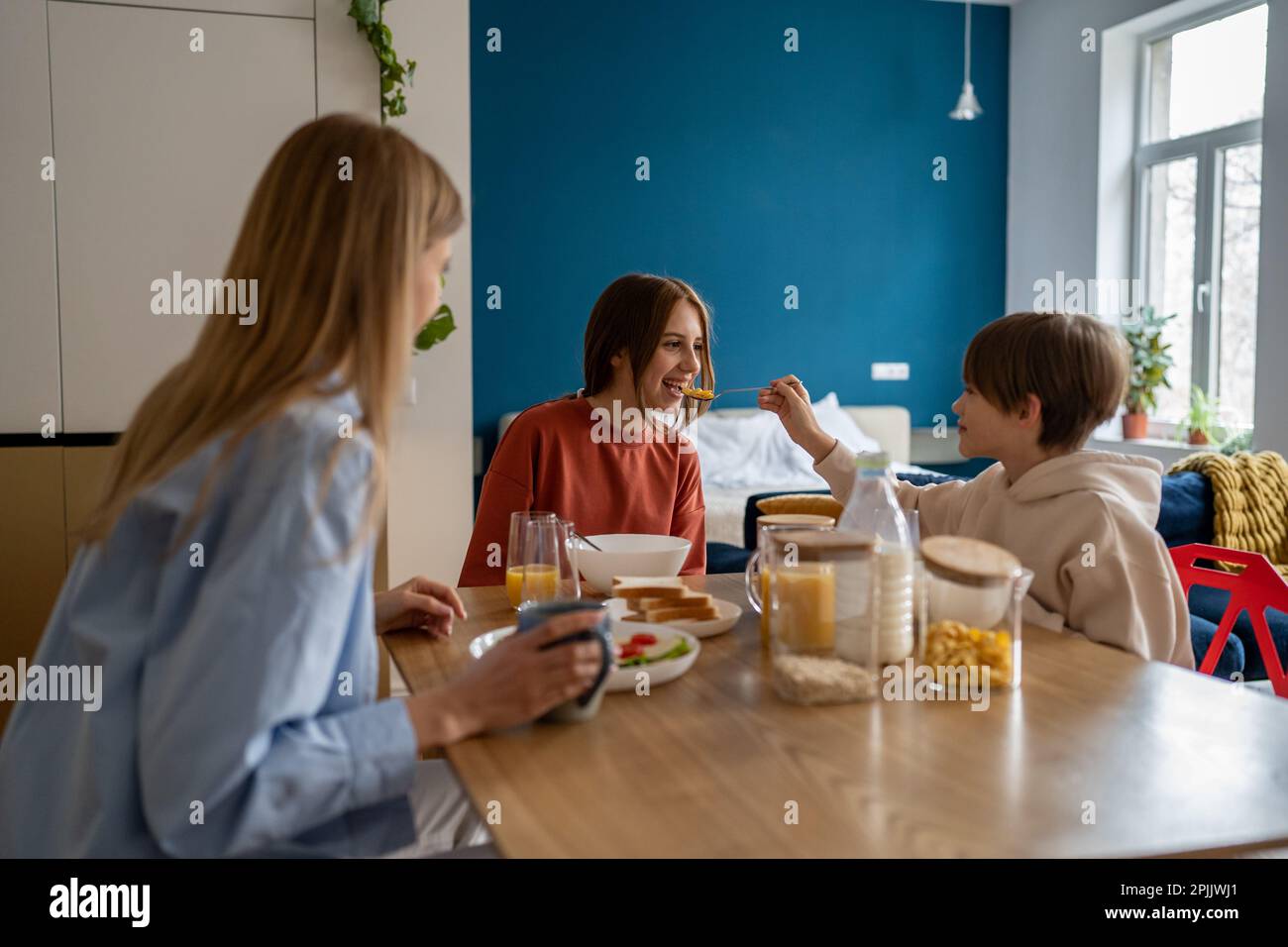 Smiling kid brother shares cornflakes with older teen sister during fun ...
