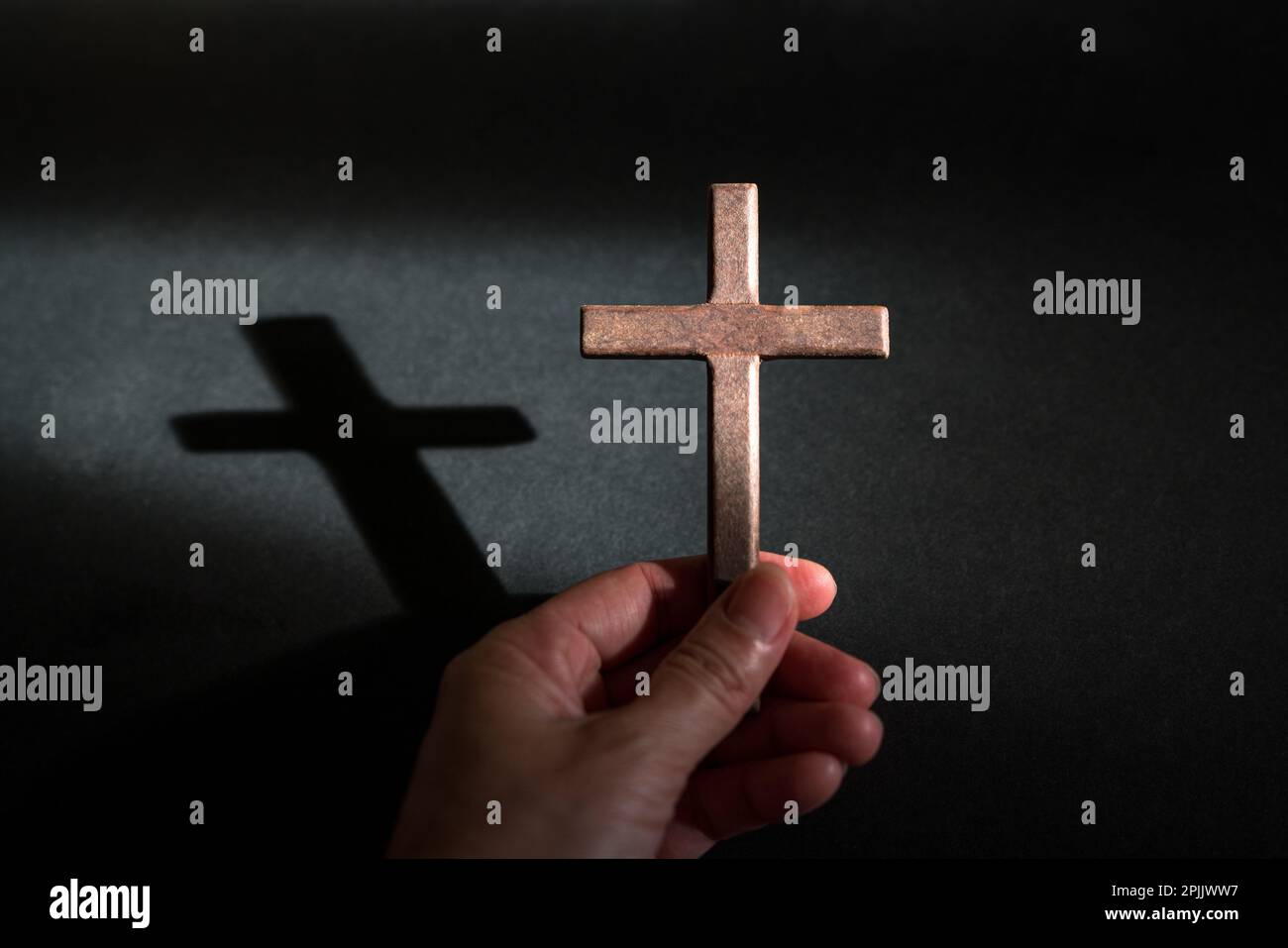 Hand holding wooden cross, with shadow on black backgorund. Copy space ...