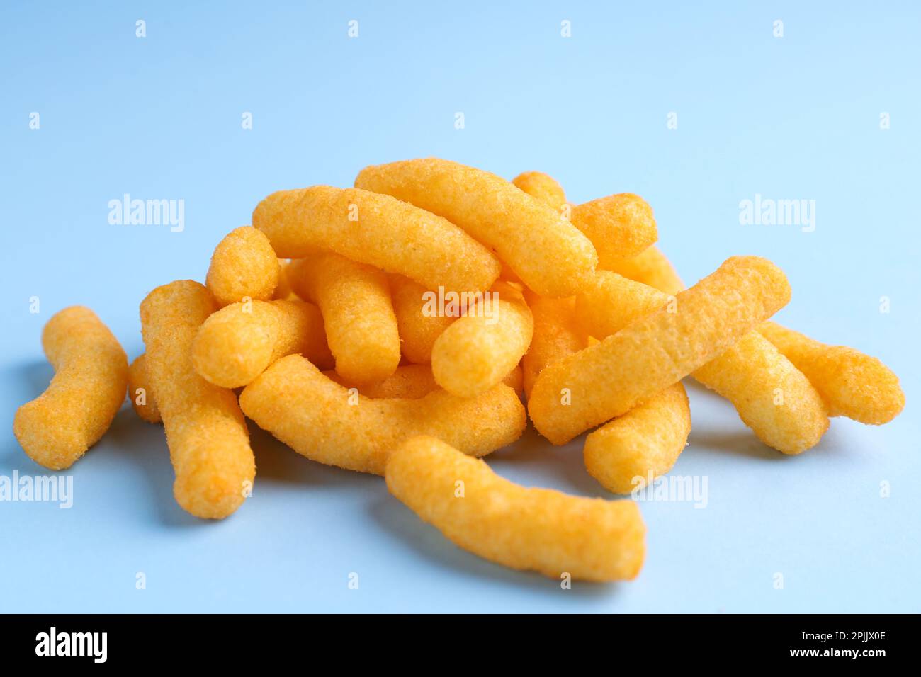 Heap of tasty cheesy corn puffs on light blue background, closeup view ...