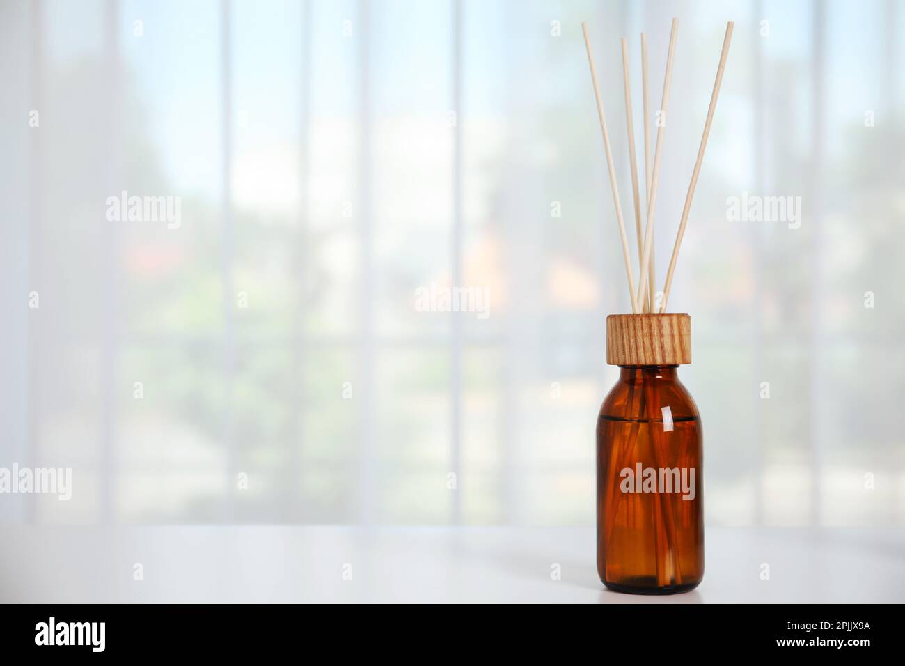 Reed diffuser on white table against window in room. Space for text ...