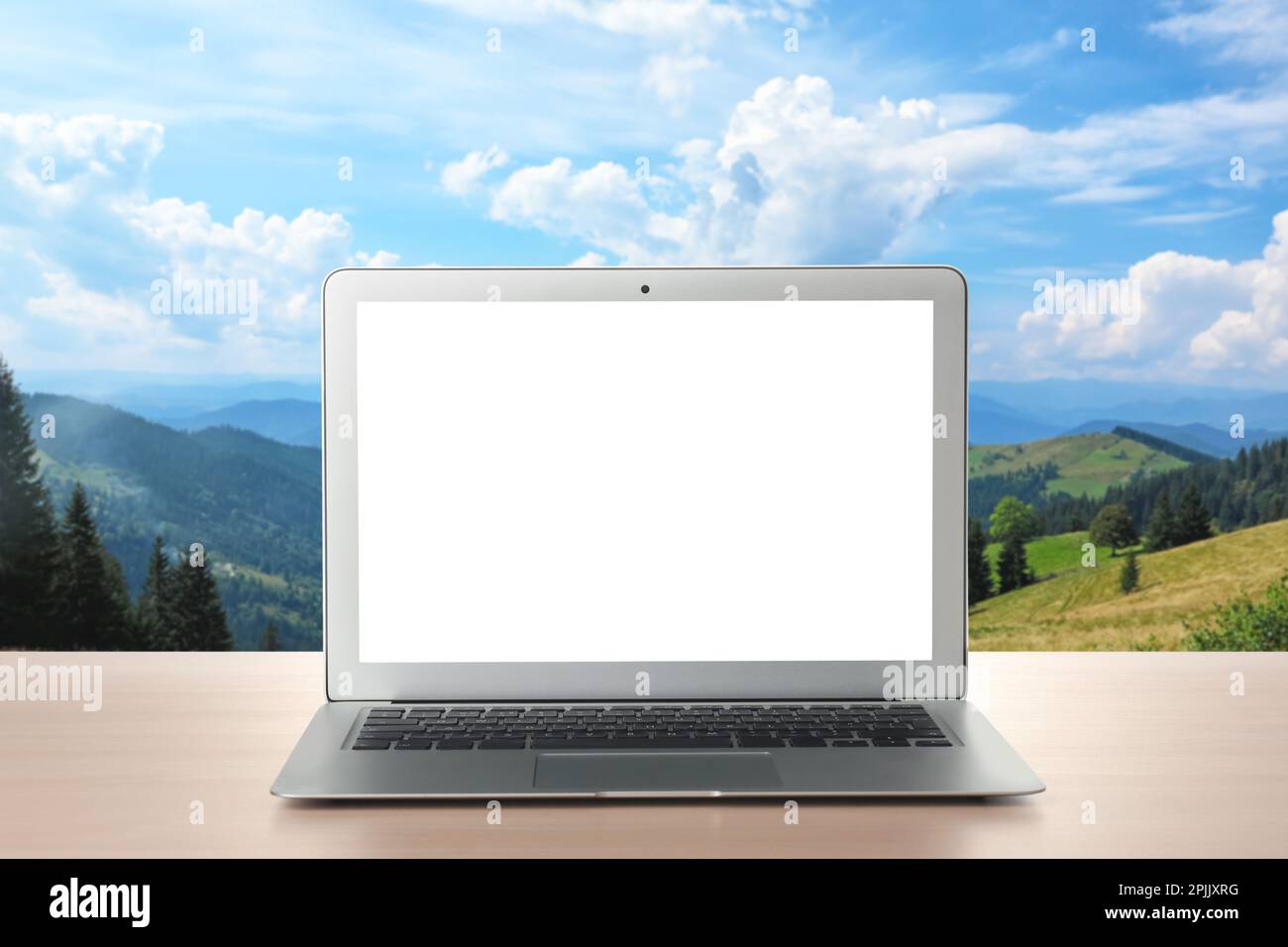 Modern laptop with blank screen on table and view of beautiful mountain ...
