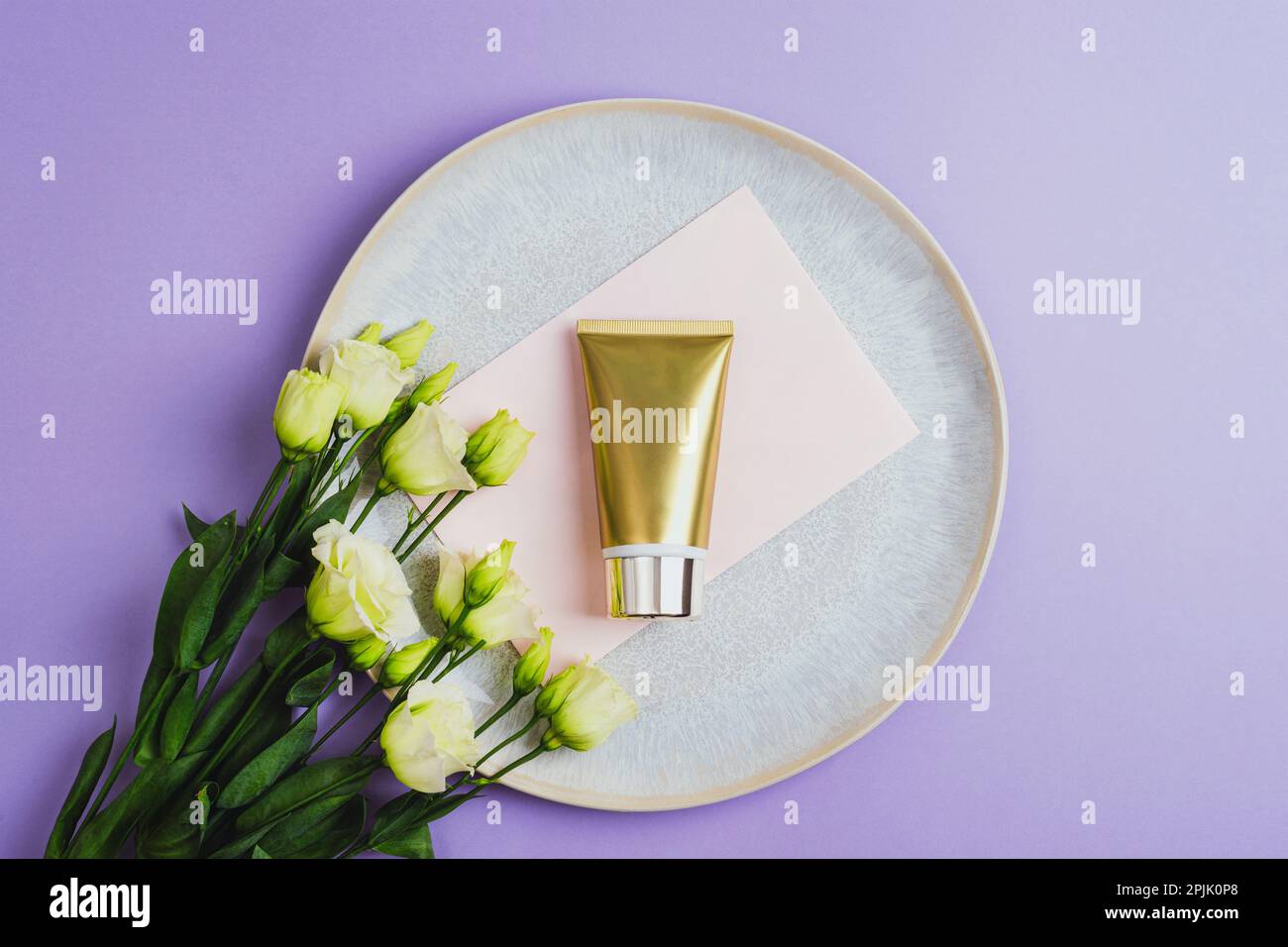 Golden cream tube and white eustoma flowers on a plate on purple ...