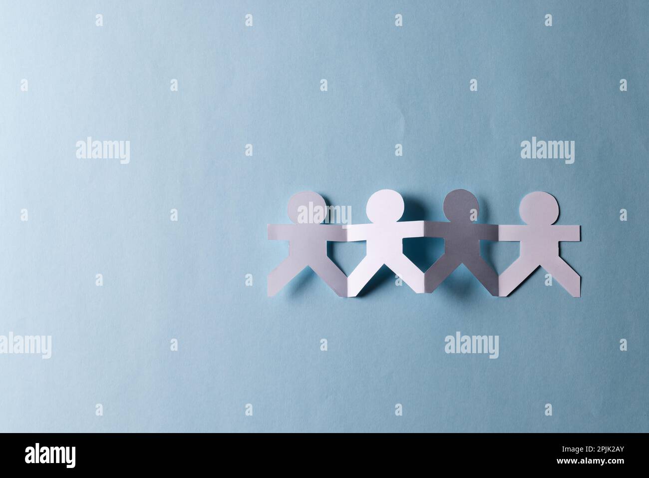 Close up of four paper cut out people figures holding hands with copy ...