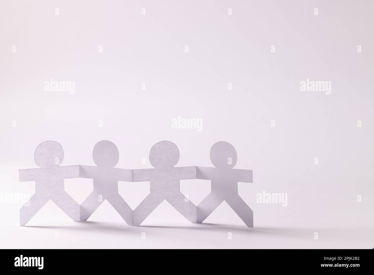 Close up of four paper cut out people figures holding hands with copy ...