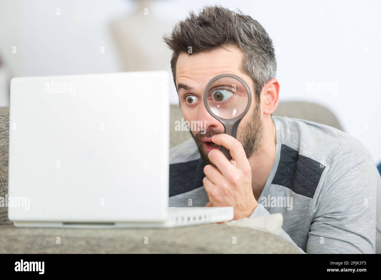 shocked man looking through a magnifying glass on his laptop Stock ...