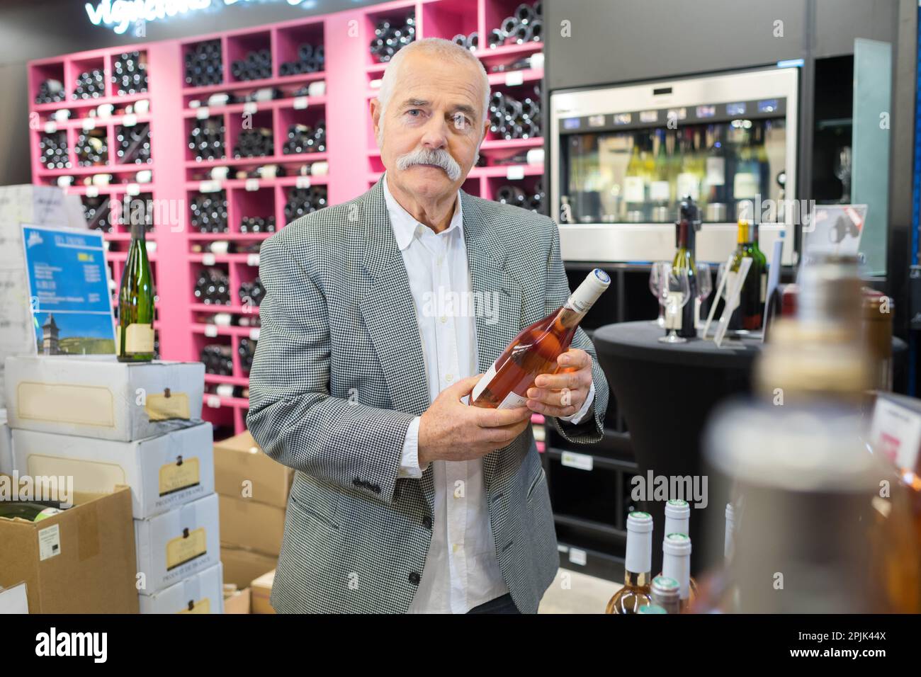man in a supermarket comparing two wine bottles Stock Photo - Alamy