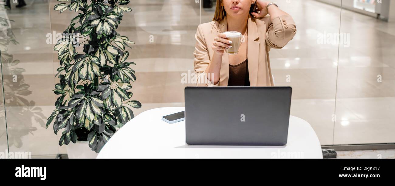 A business woman sits in a cafe, works at a computer, drinks coffee ...