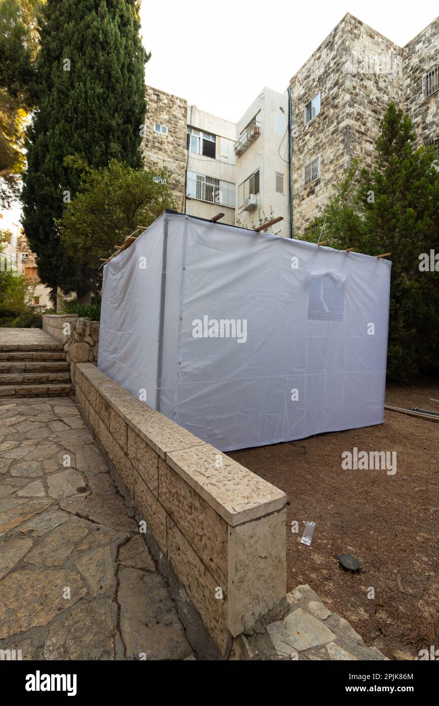 A white sukkah is being built in the yard of a residential building in ...