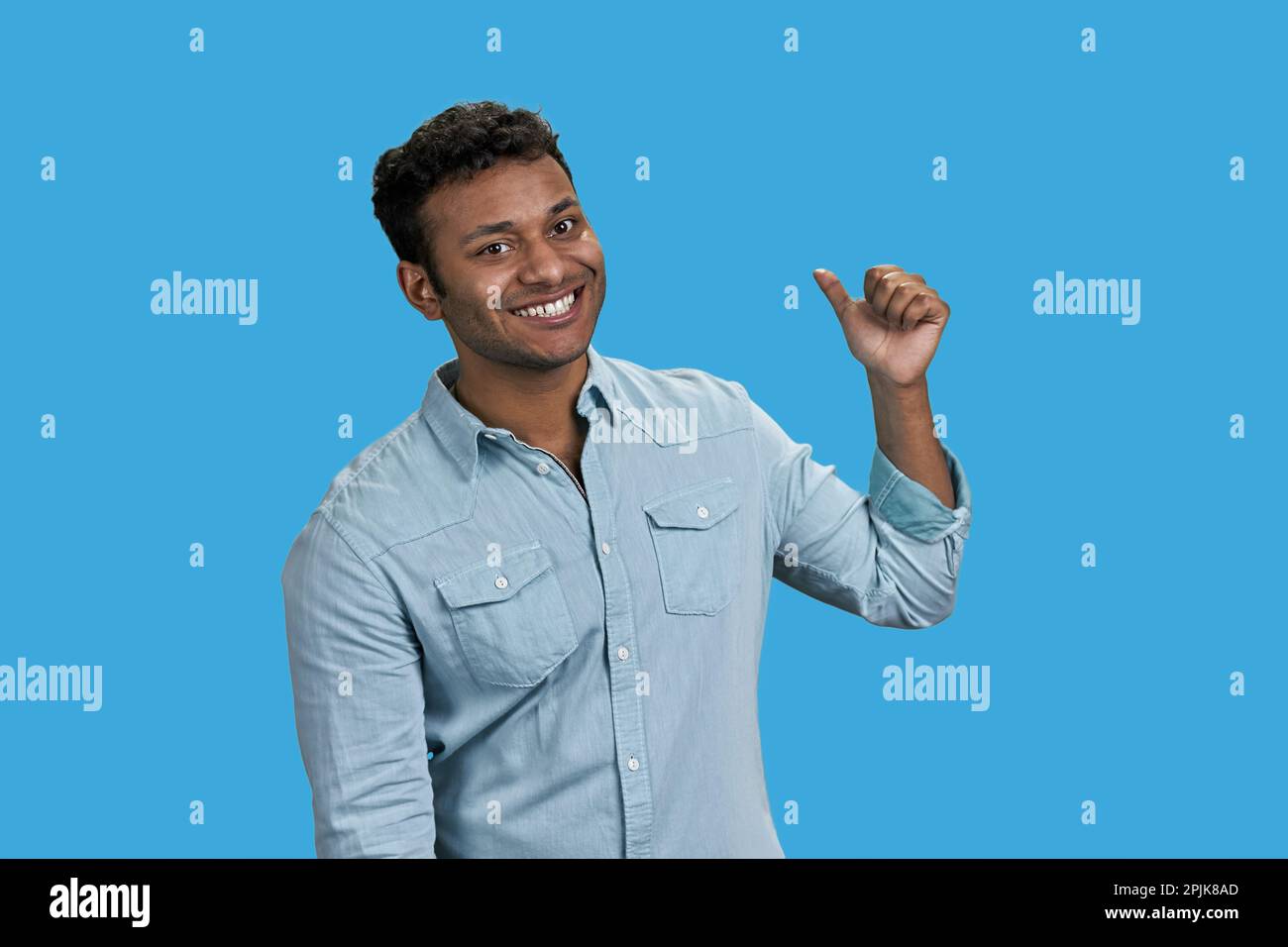Young smiling south asian man is pointing back with thumb. Isolated on ...
