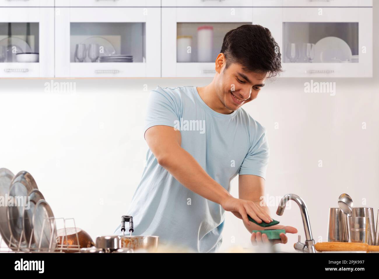 Cheerful man washing utensils with dish wash bar in kitchen at home ...