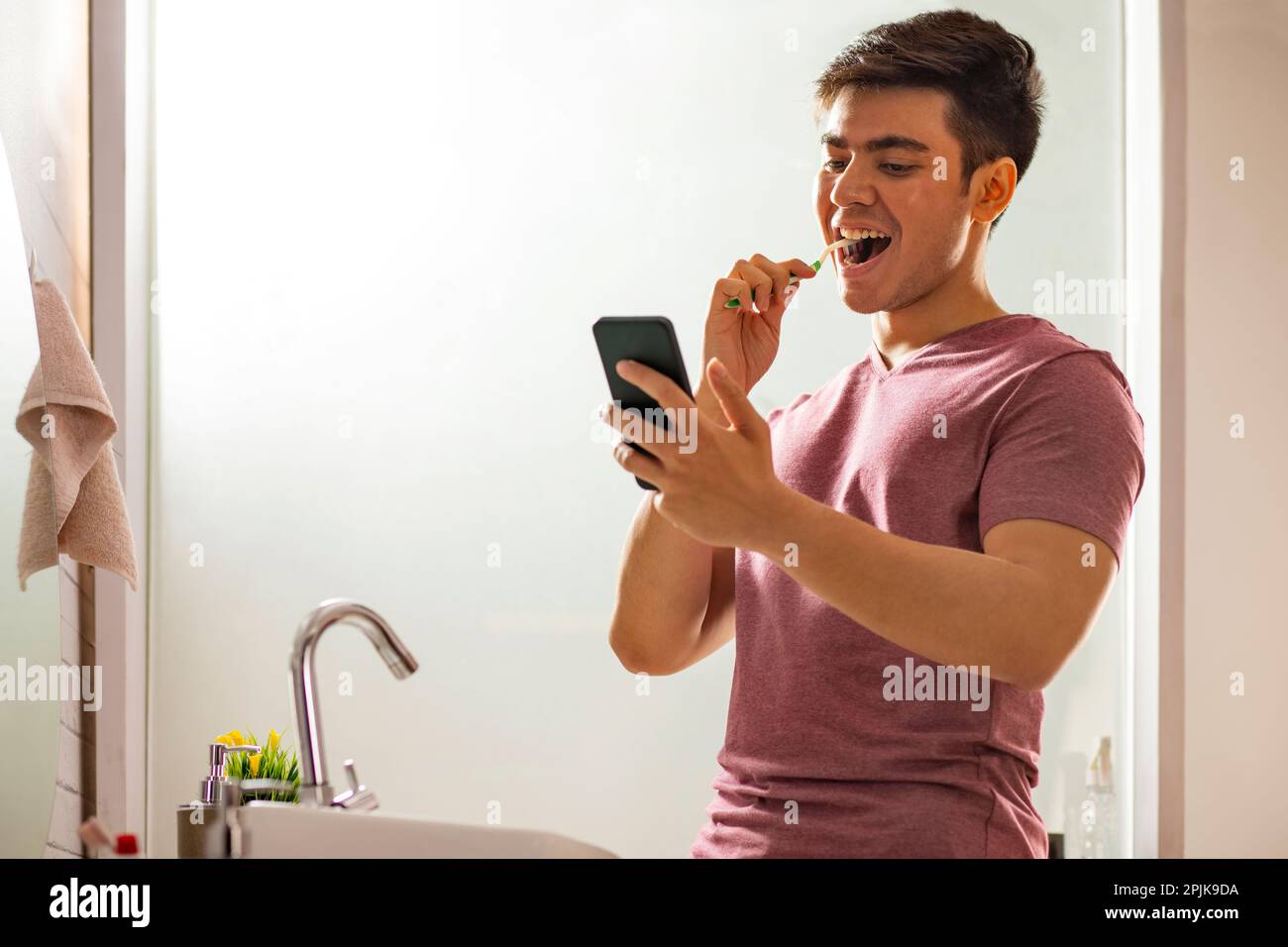 Young man using mobile phone while brushing teeth in bathroom Stock ...