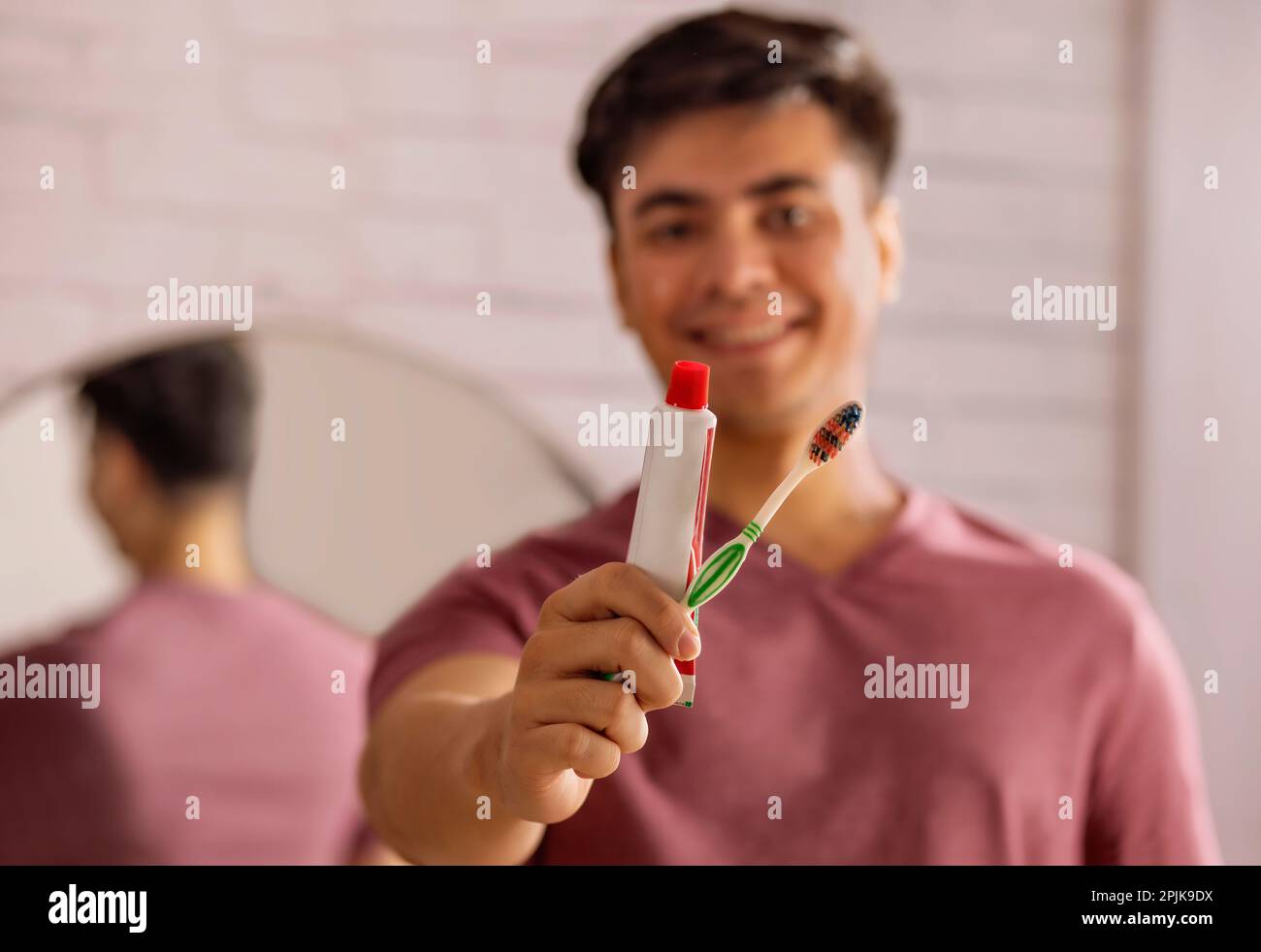 Young man holding toothbrush and toothpaste in bathroom Stock Photo - Alamy