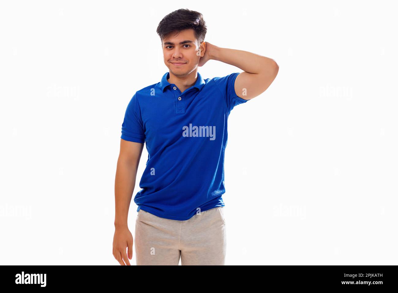 Portrait of young man standing with hand behind head against white ...