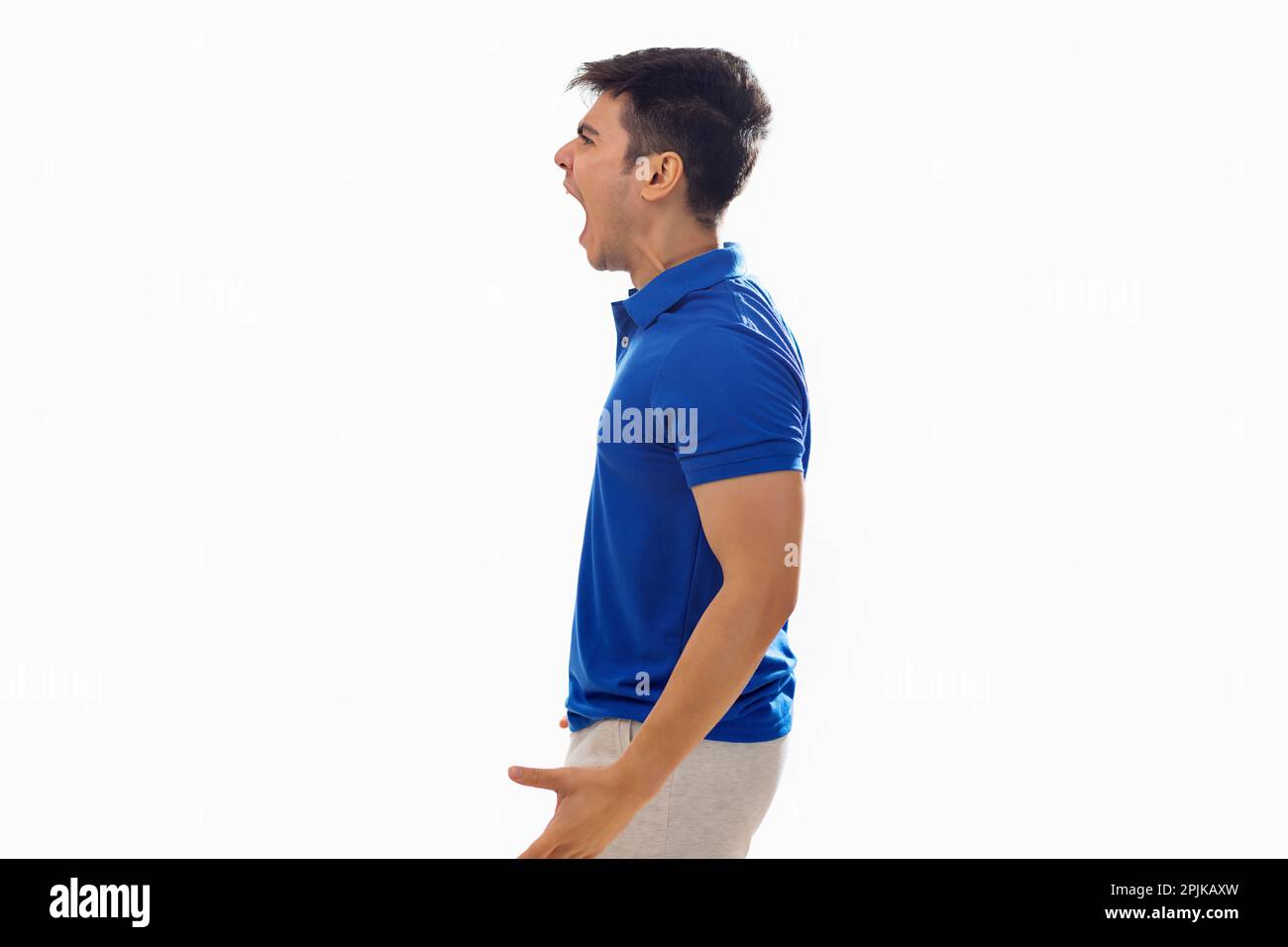 Side View of an angry young man screaming while standing against white ...