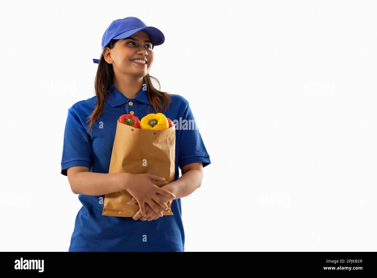 Side view of delivery woman holding a bag of fresh vegetable against ...