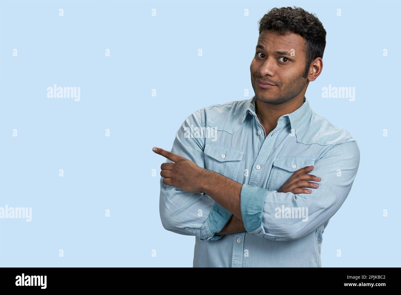 South asian brown guy with folded arms pointing at copy space. Isolated ...