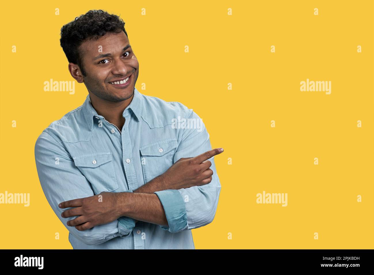 Indian man with folded arms pointing at copy space on the right ...