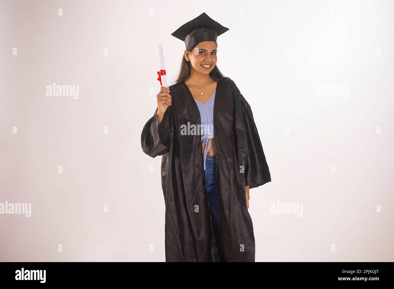 Portrait of young woman in graduation gown holding certificate while ...