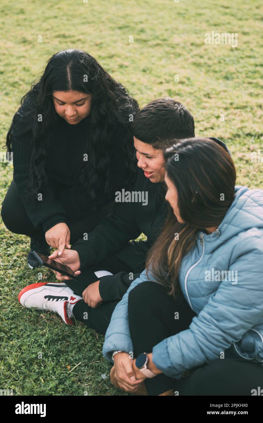 three people of Hispanic-Latino ethnicity, sitting on the ground in the ...