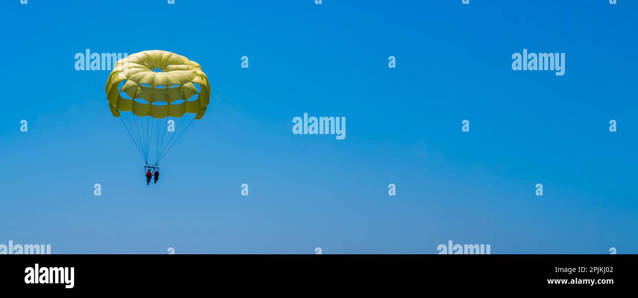 Parasailing on a yellow parachute against the blue sky. Beach extreme ...