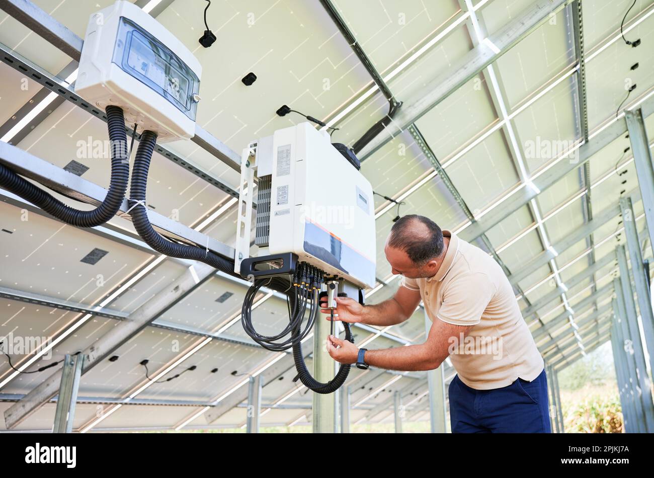 Young man adjusting hybrid inverter. Worker connecting wires to PV ...